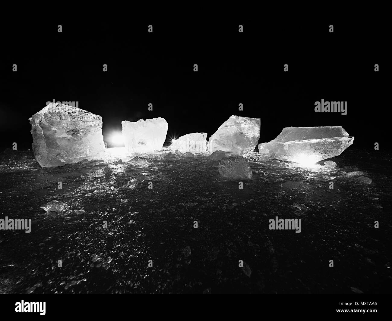 Ice cubes on a dark reflective ground. Glowing pieces of chopped ice ...