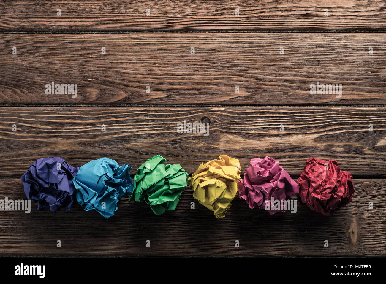 Set of multiple colorful crampled paper ball placed in line on wooden ...