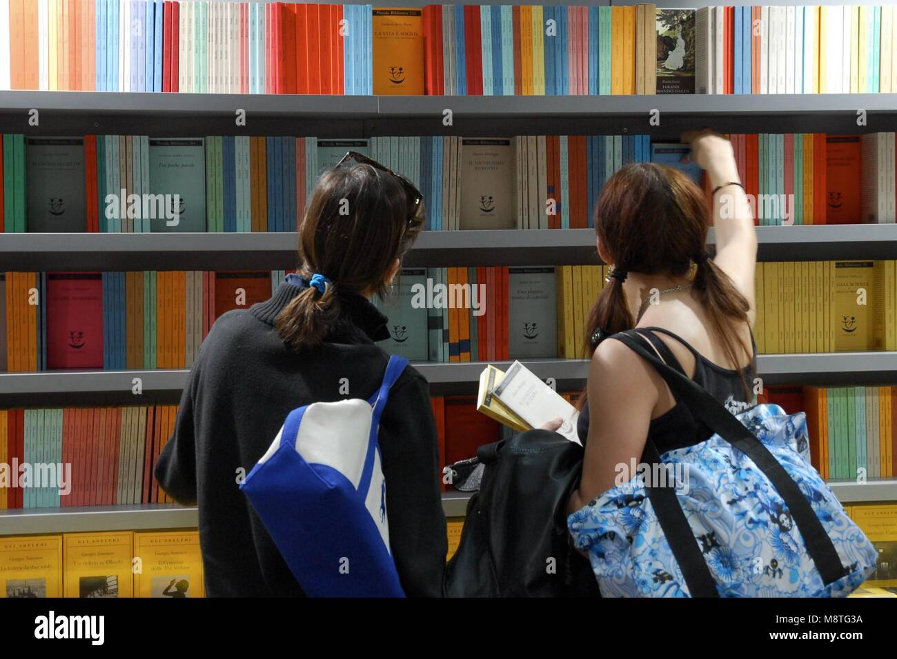 Women back view picking books from shelves in a book fair Turin Italy ...