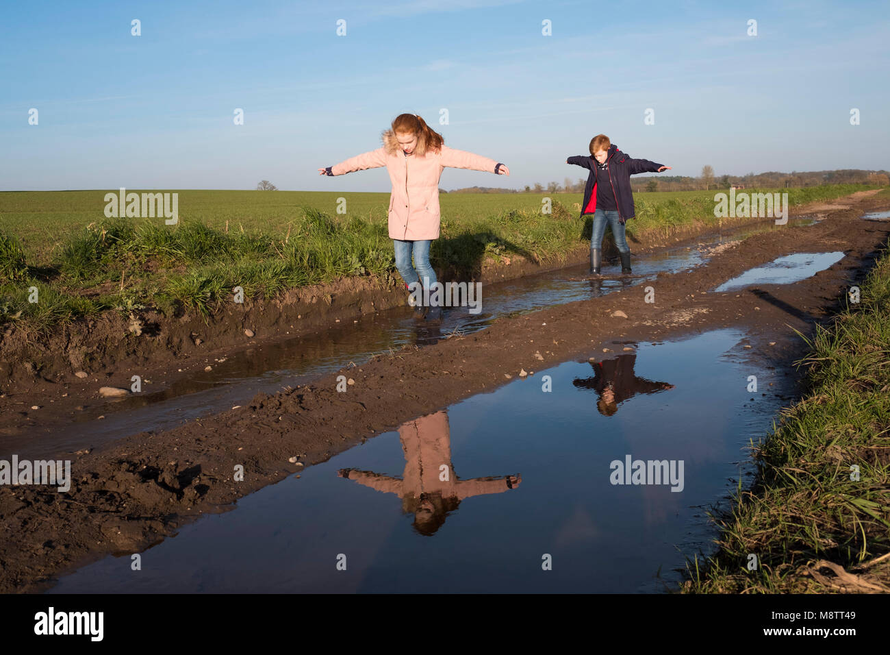 A teenage boy and girl splashing in puddles of mud on a country walk ...