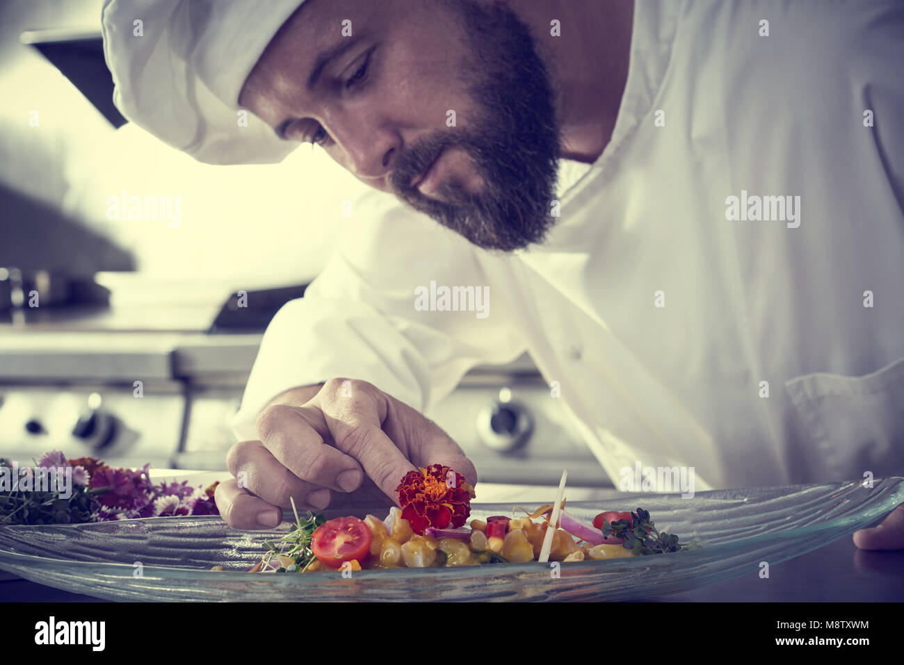 Chef garnishing flower in ceviche dish with hands at stainless steel ...
