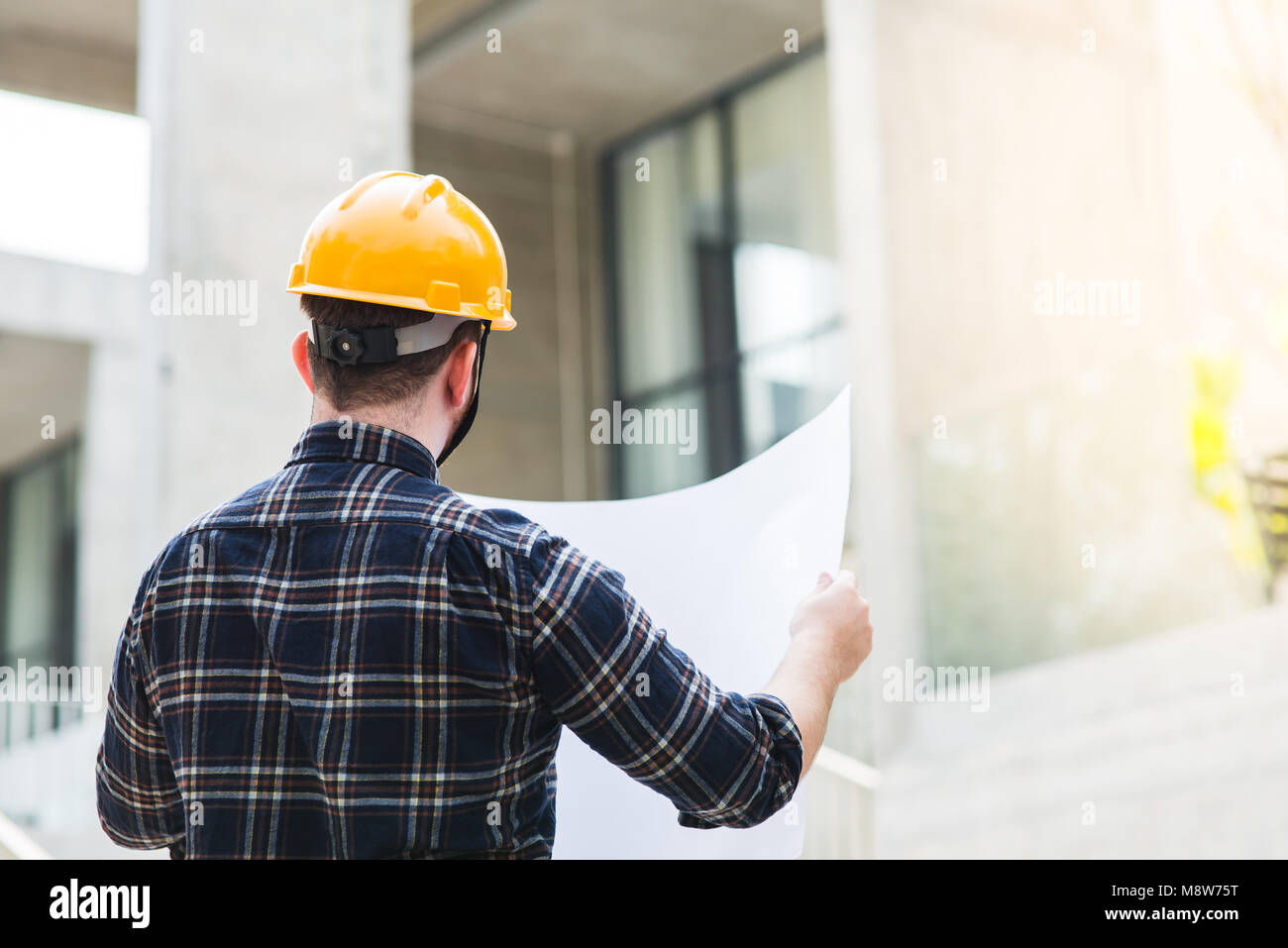 Back of engineer holding blueprint with building background Stock Photo ...