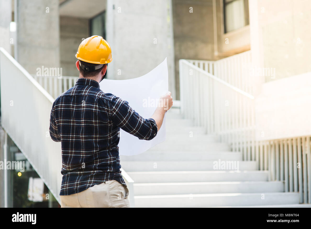 Back of engineer holding blueprint with building background Stock Photo ...