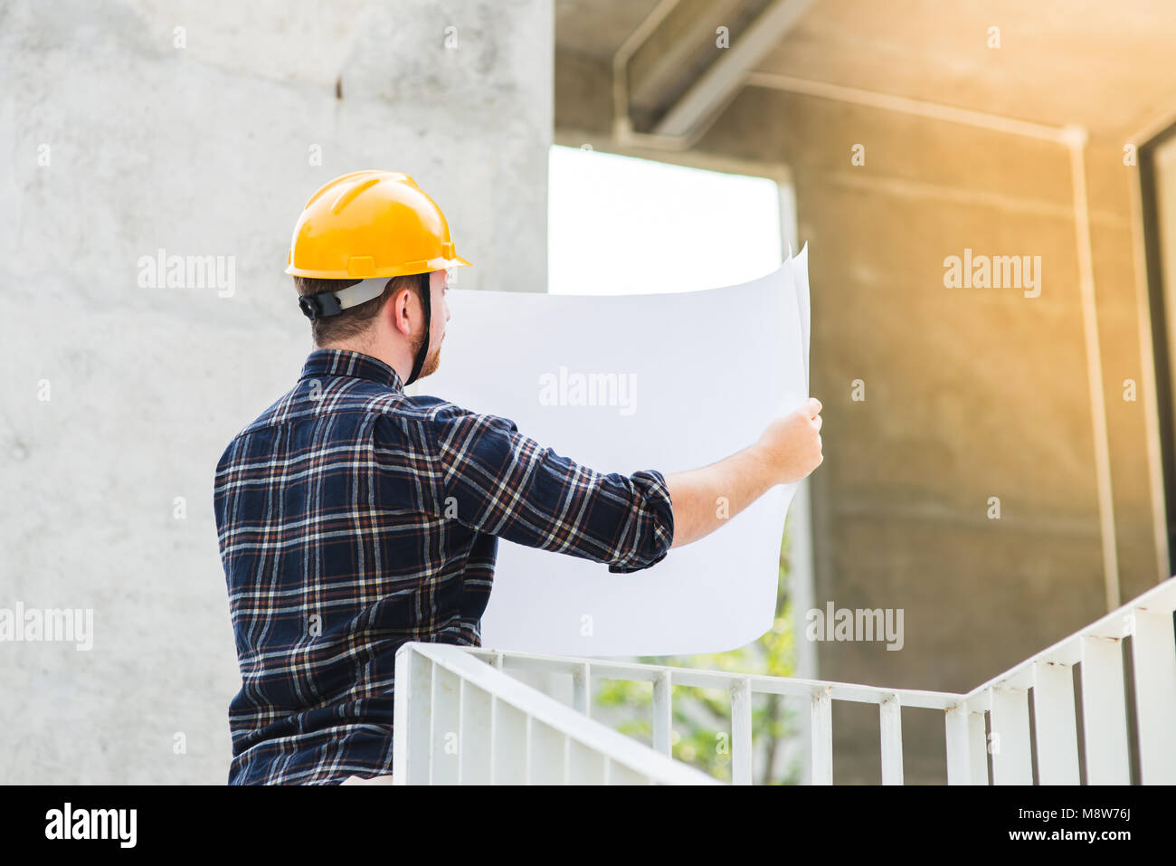 Back of engineer holding blueprint with building background Stock Photo ...