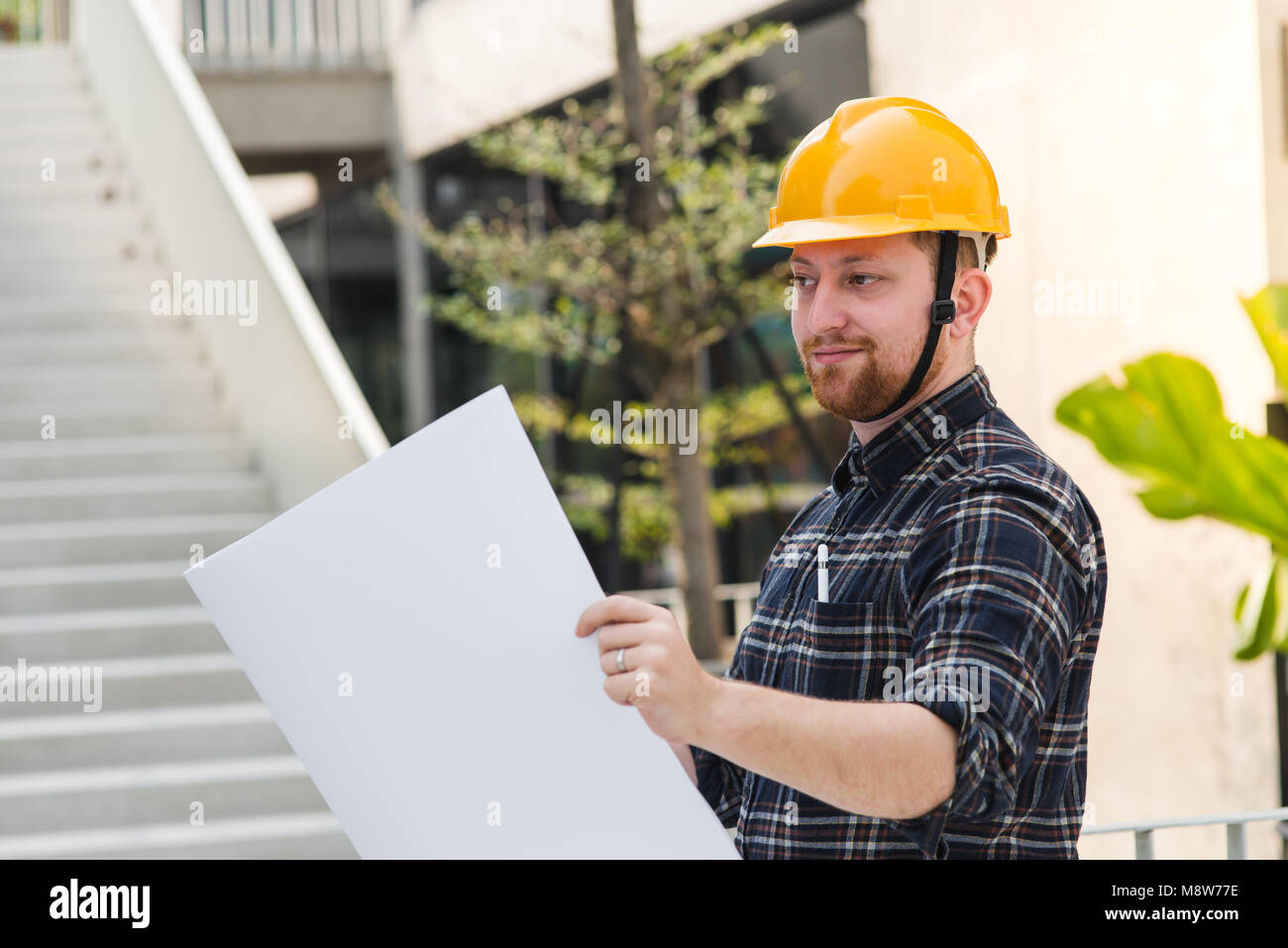 Back of engineer holding blueprint with building background Stock Photo ...
