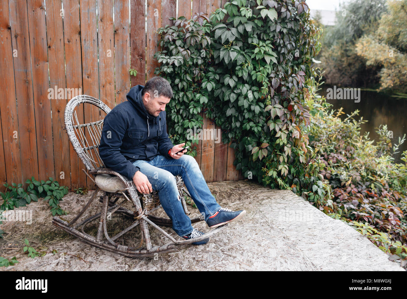 Handsome man relax in vintage rocking-chair with phone in garden Stock ...