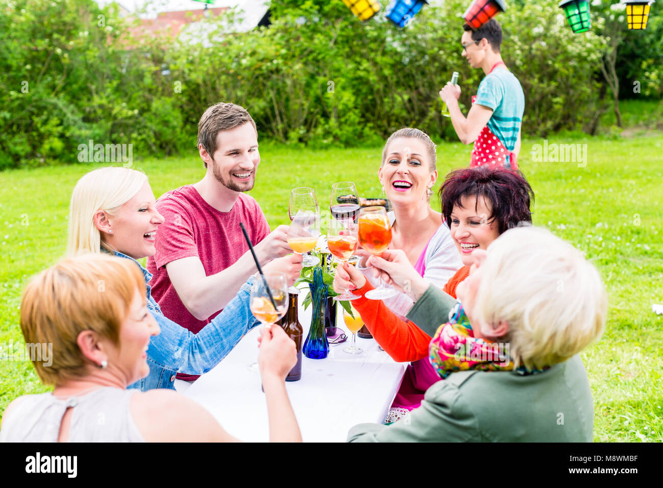 People toasting at party, in the background man at bbq grill with beer ...