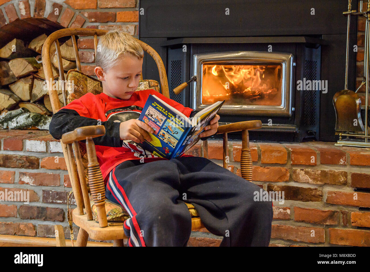 Blond boy reading a book by the fireplace Stock Photo - Alamy