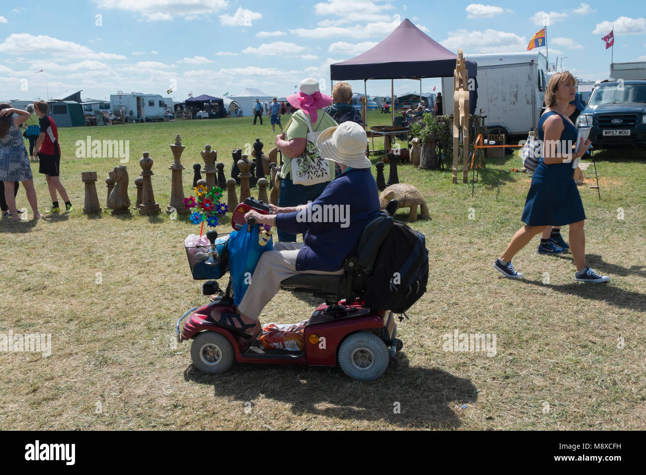 Woman in a mobility scooter driving past a big wooden chess set by a ...