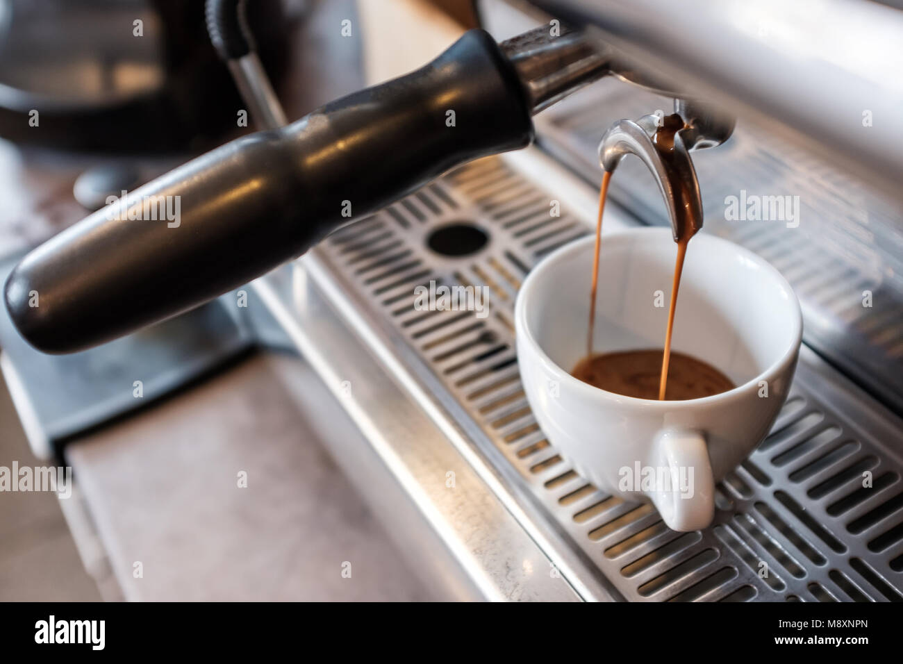 Fresh espresso dripping from portafilter of coffee machine into white ...