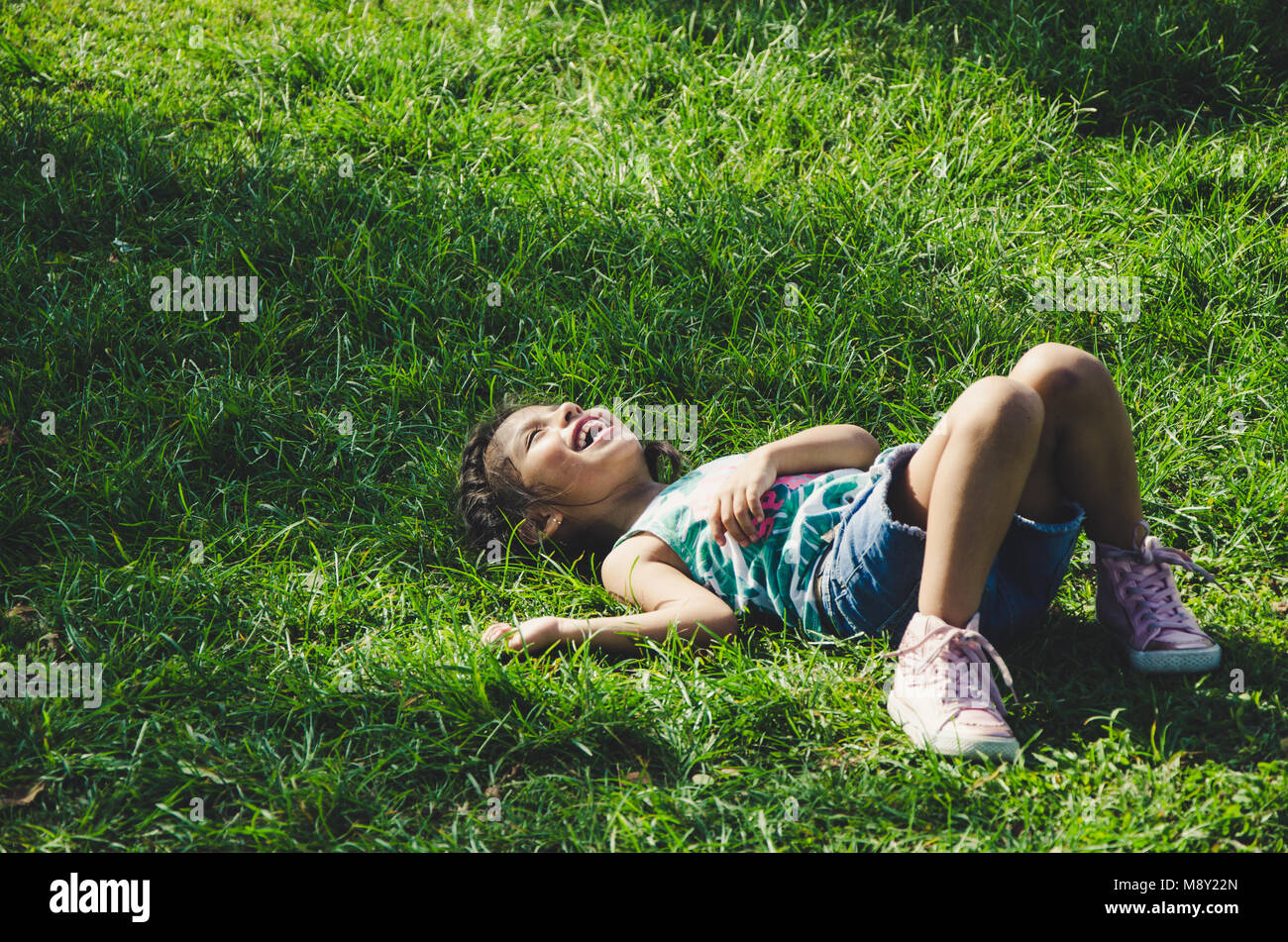 Laughing little girl lying on the grass in the park Stock Photo - Alamy