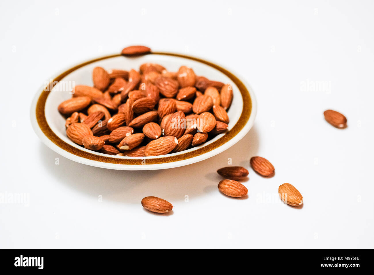 A small plate of almonds plain white background Stock Photo - Alamy