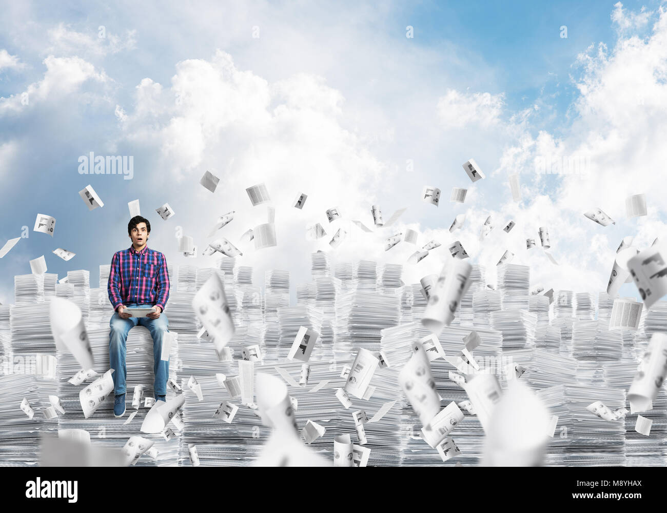 Young man in casual clothing sitting on pile of documents among flying ...