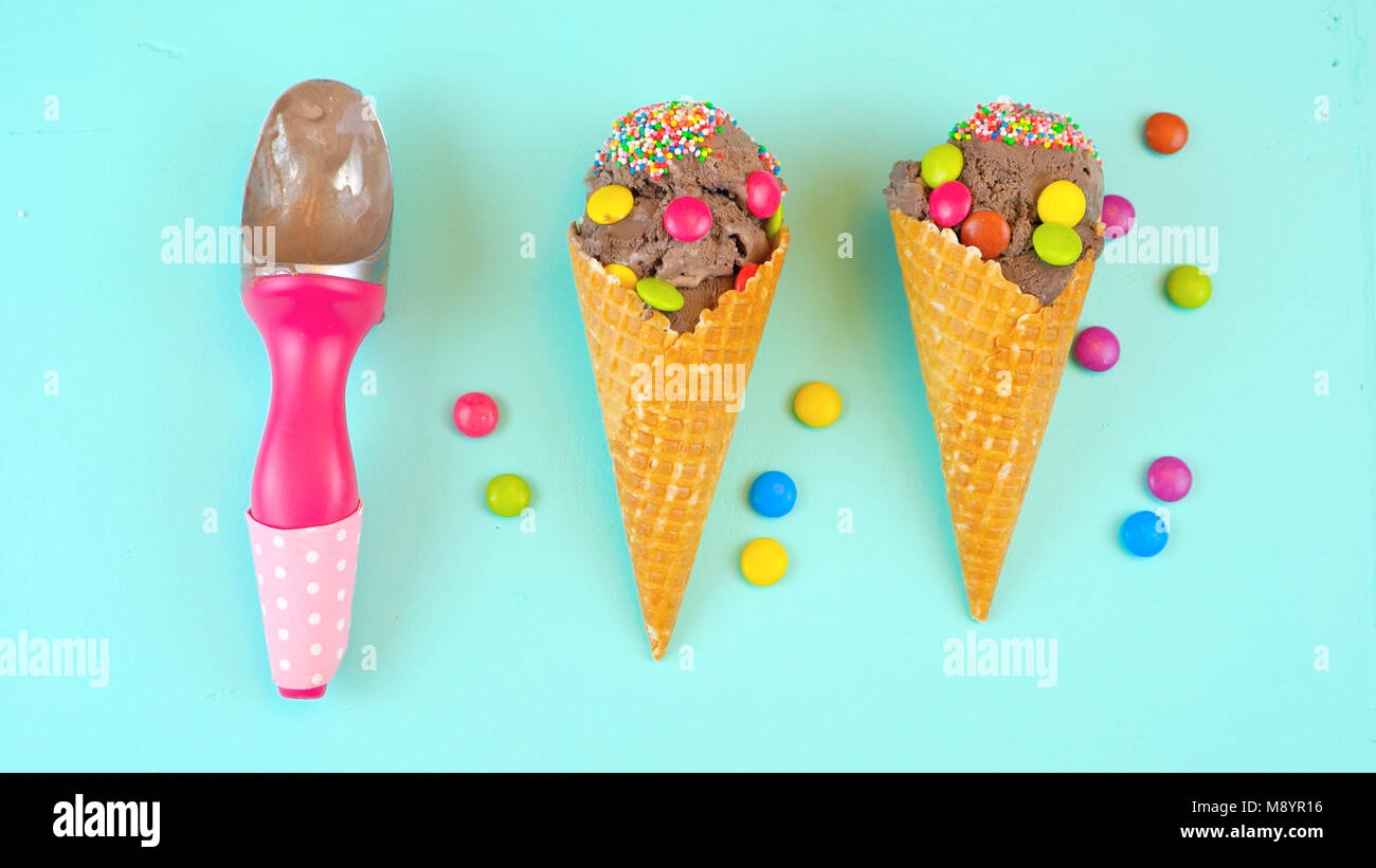 Chocolate ice cream cones decorated with candy, on blue wood table ...