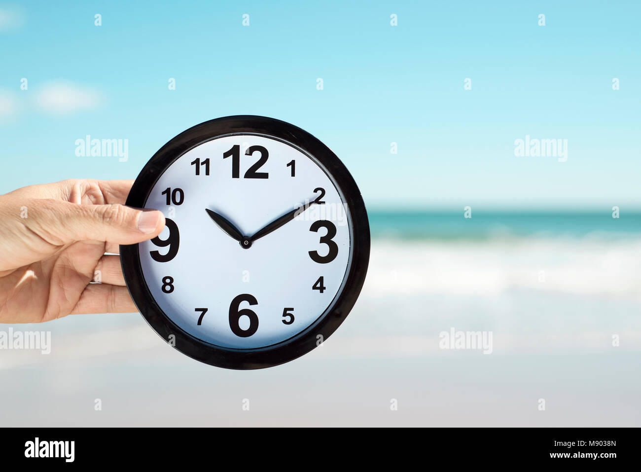 closeup of a young caucasian man with a clock in his hand on the beach ...
