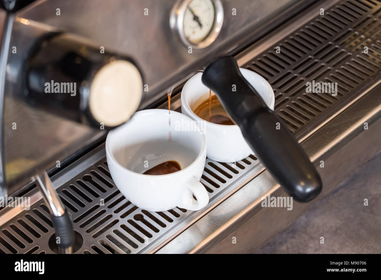 Fresh espresso dripping from portafilter of coffee machine into white ...