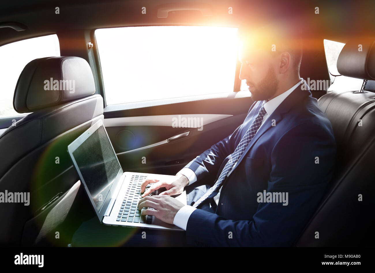 Side view of a businessman using a laptop in the backseat of a car ...
