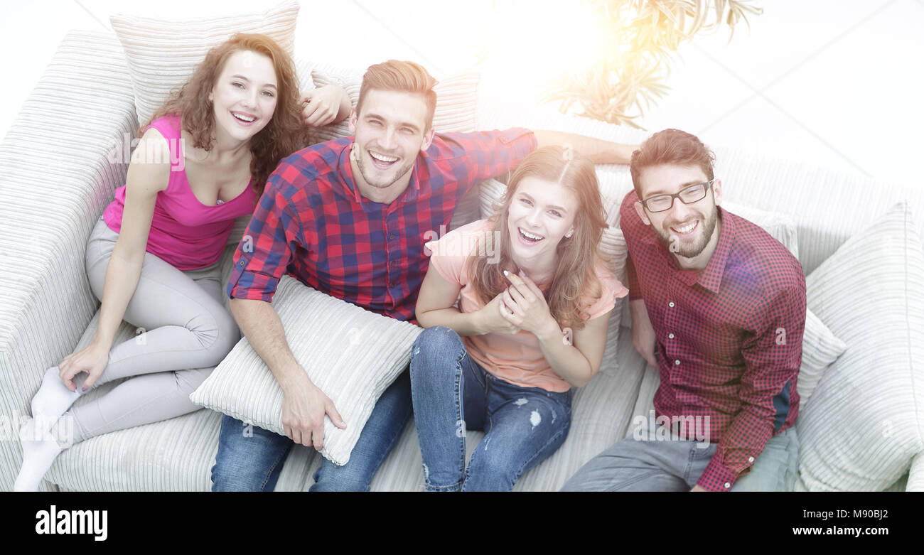 four friends laugh, sitting on the sofa and looking at camera Stock ...