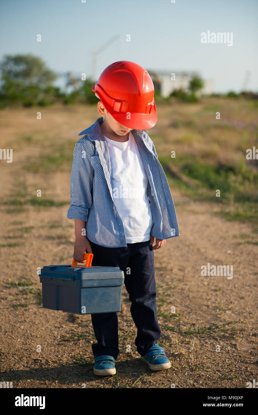 sad little working kid in orange helmet hung his head with tool case in ...