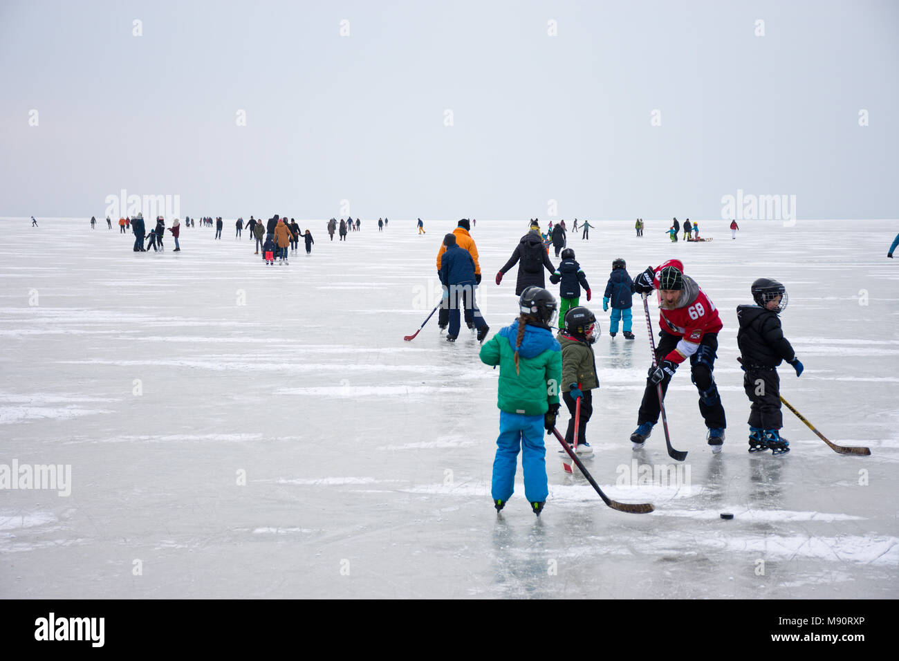 Father and children playing ice hockey amongst other ice skating people ...