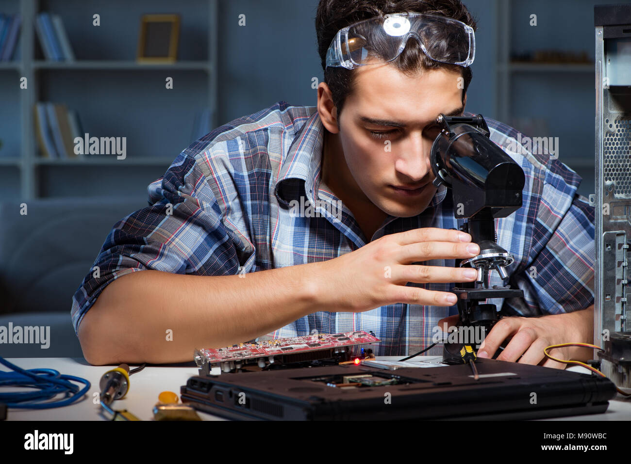 Repairman trying to repair laptop with miscroscope Stock Photo - Alamy