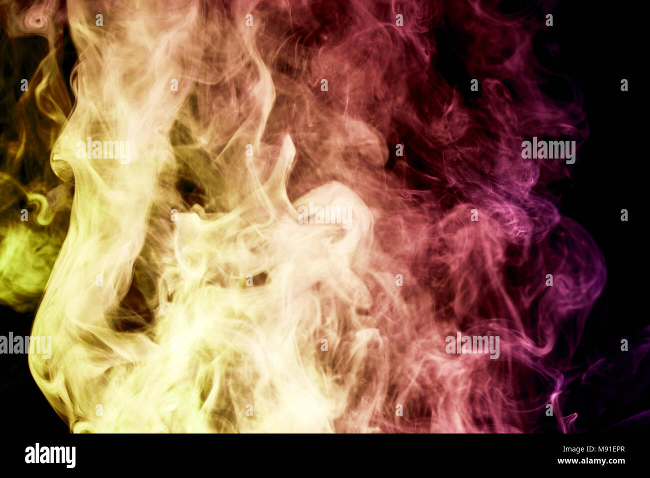 Thick colorful smoke of yellow and pink on a black isolated background ...