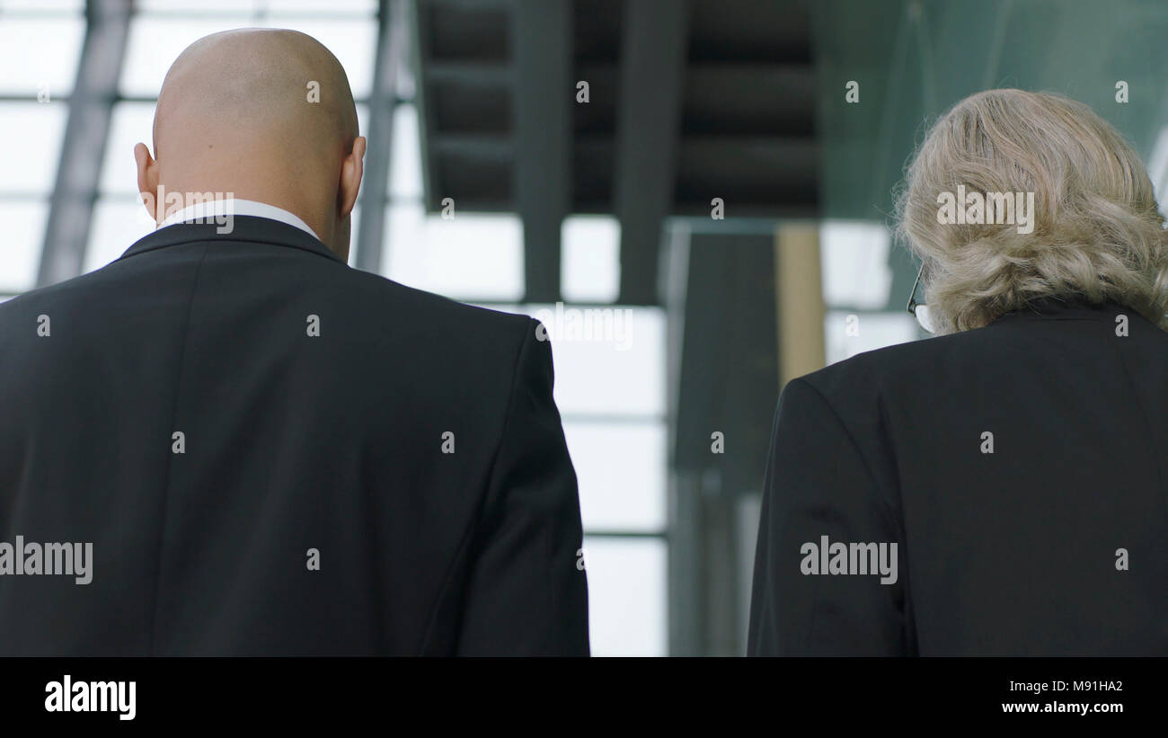 rear view of corporate executives talking while ascending stairs in ...
