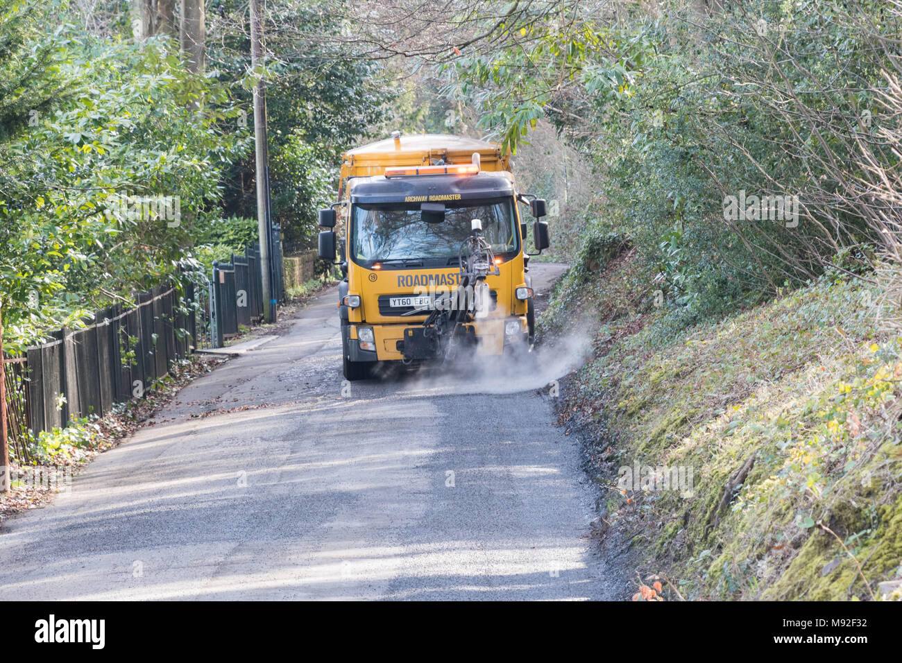 A pothole repair vehicle works a damaged country lane repairing winter ...
