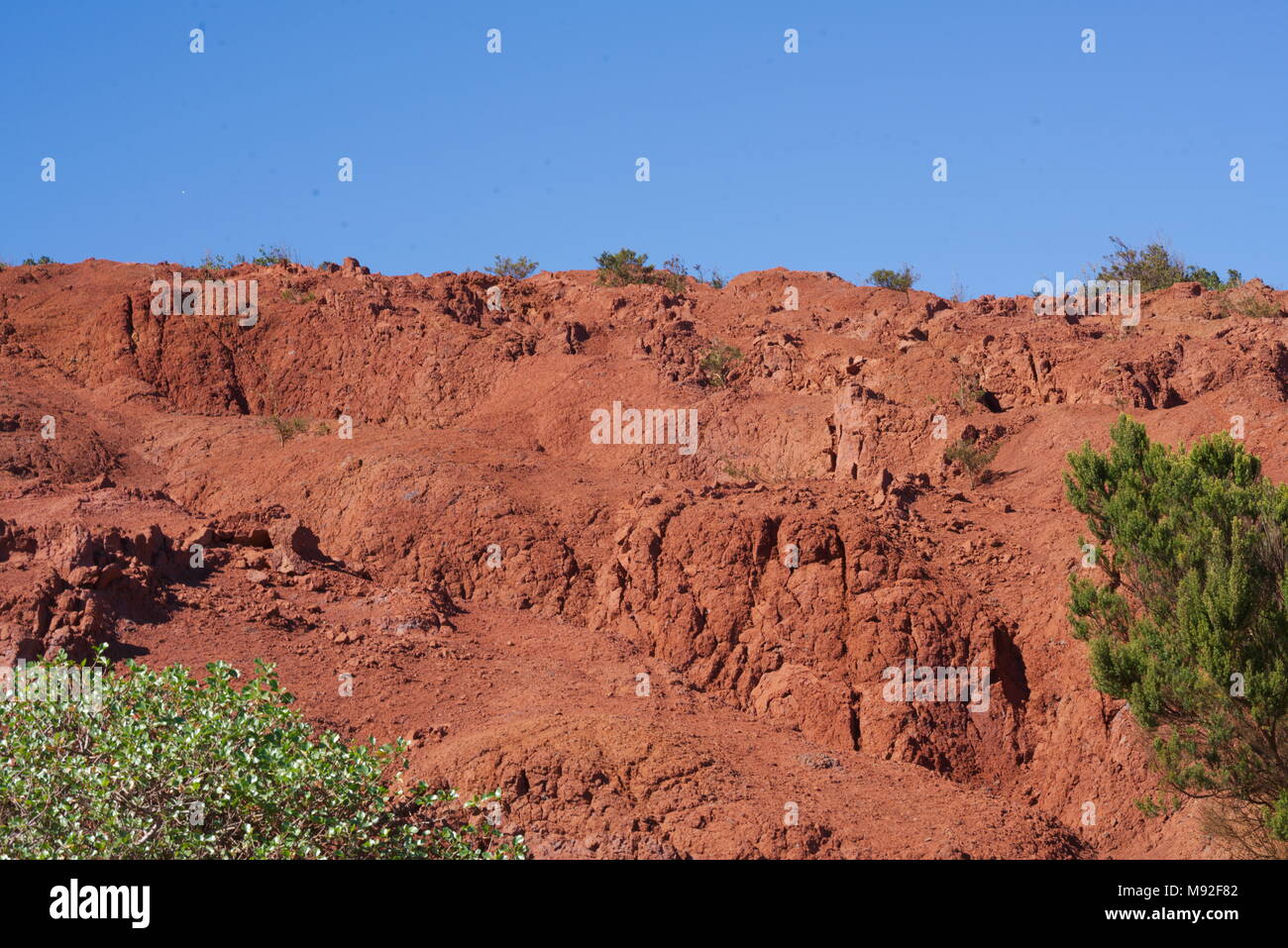red rock background with a blue sky and some green bushes Stock Photo ...