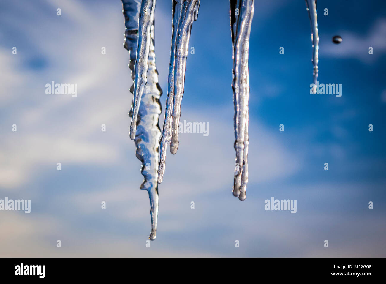Large icicles on a house roof, blue sky and clouds in background ...