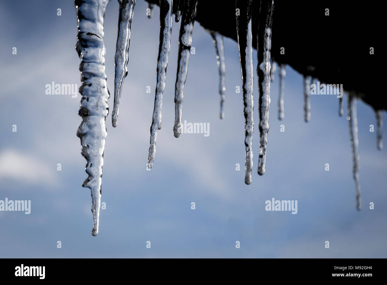 Large icicles on a house roof, blue sky and clouds in background ...