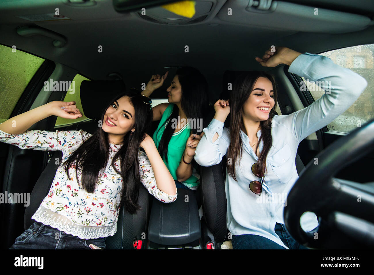 Three girls driving in a car dancing and having fun in city street ...