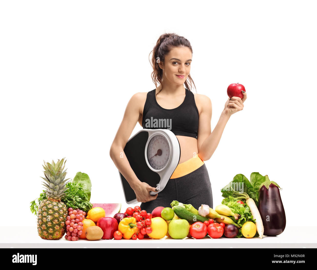 Fitness woman with a weight scale and an apple behind a table with ...