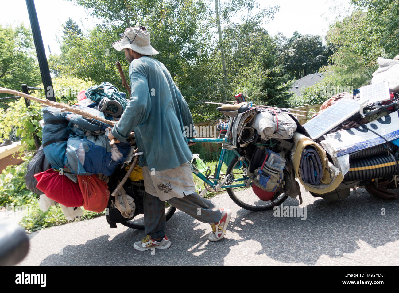 Homeless man walking beside his bicycle and cart stacked high with all ...
