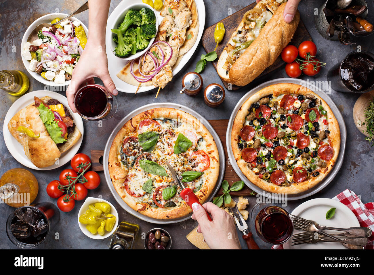 Big dinner with pizza, salad and sandwiches with hands reaching food ...