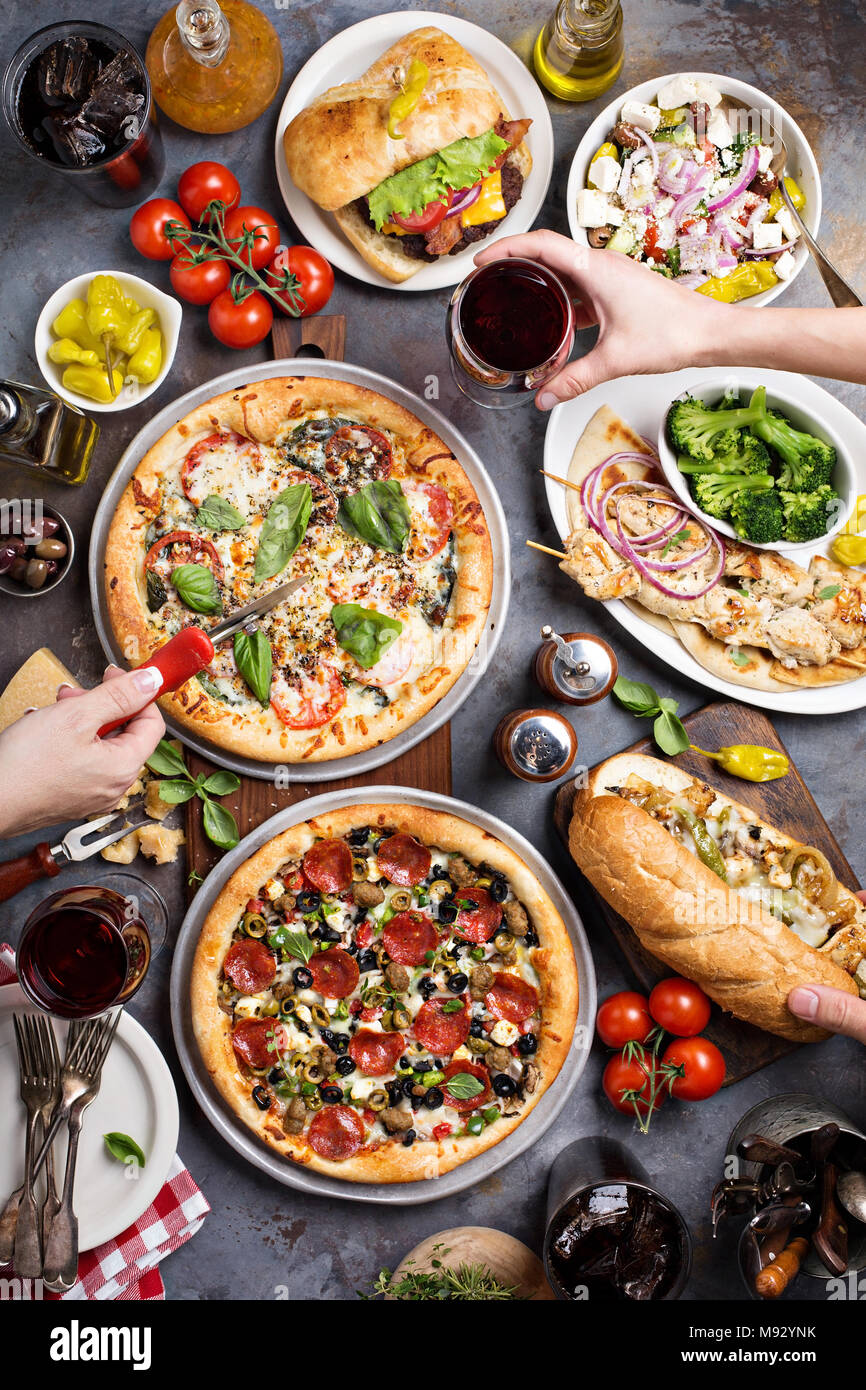 Big dinner with pizza, salad and sandwiches with hands reaching food ...