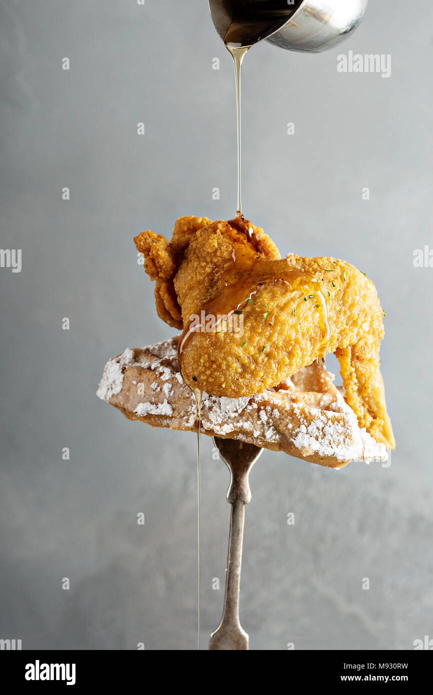 Fried chicken wing with a waffle on a fork with syrup pouring over ...
