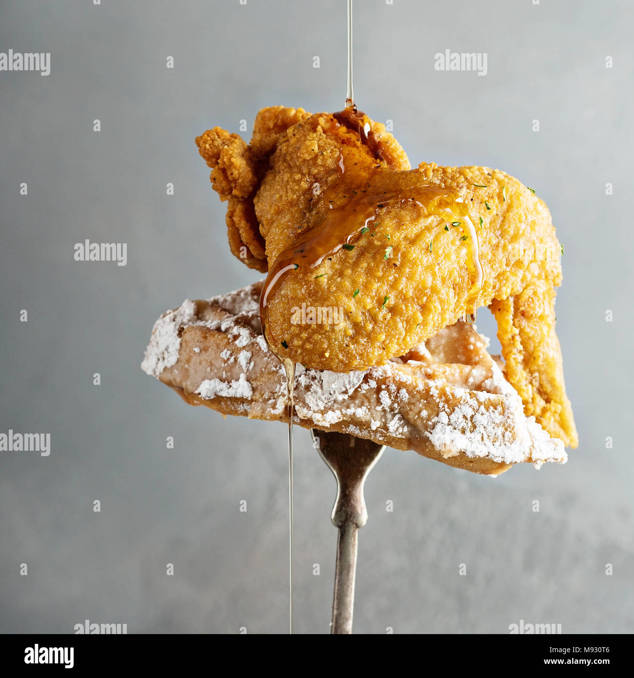 Fried chicken wing with a waffle on a fork with syrup pouring over ...