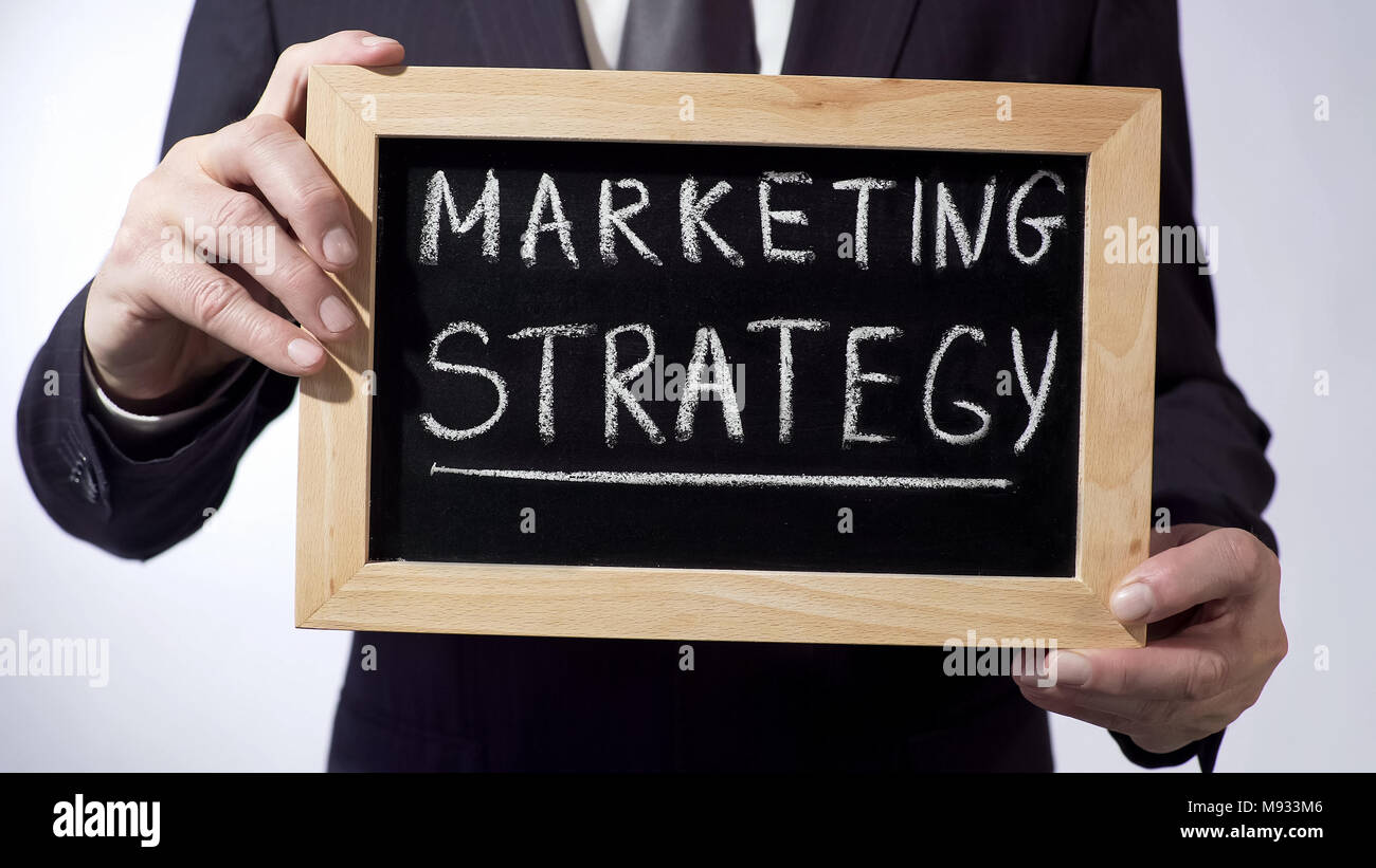 Marketing strategy written on blackboard, businessman holding sign ...