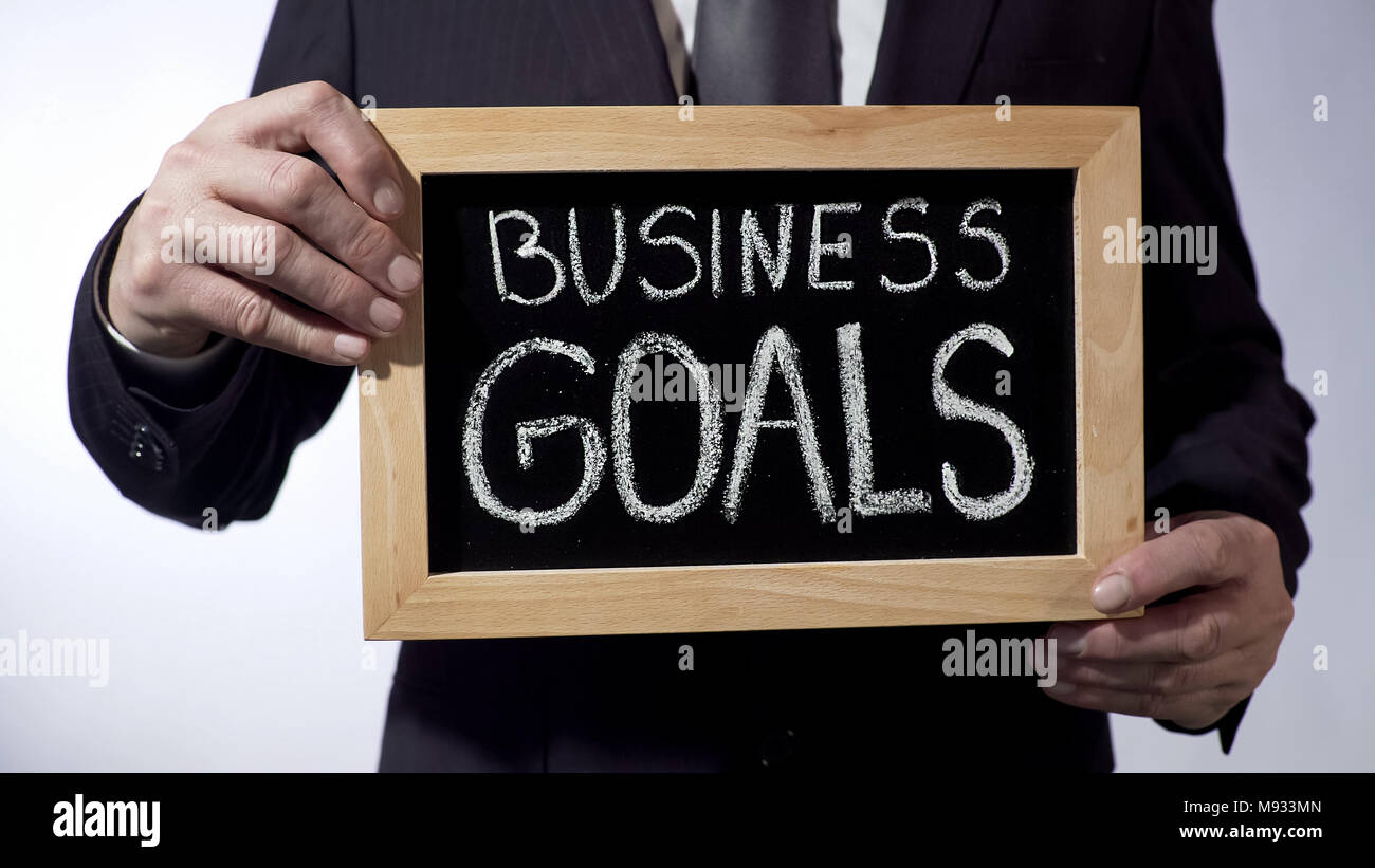 Business goals written on blackboard, businessman holding sign ...
