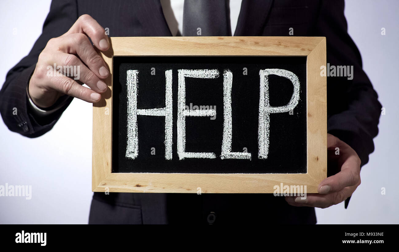 Help written on blackboard, man wearing black suit holding sign ...