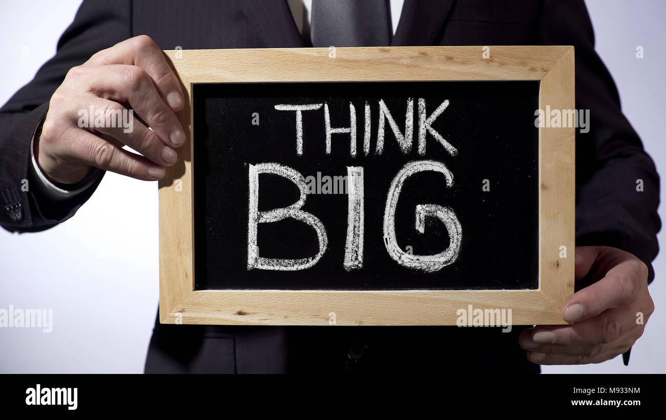 Think big written on blackboard, male in suit holding sign ...