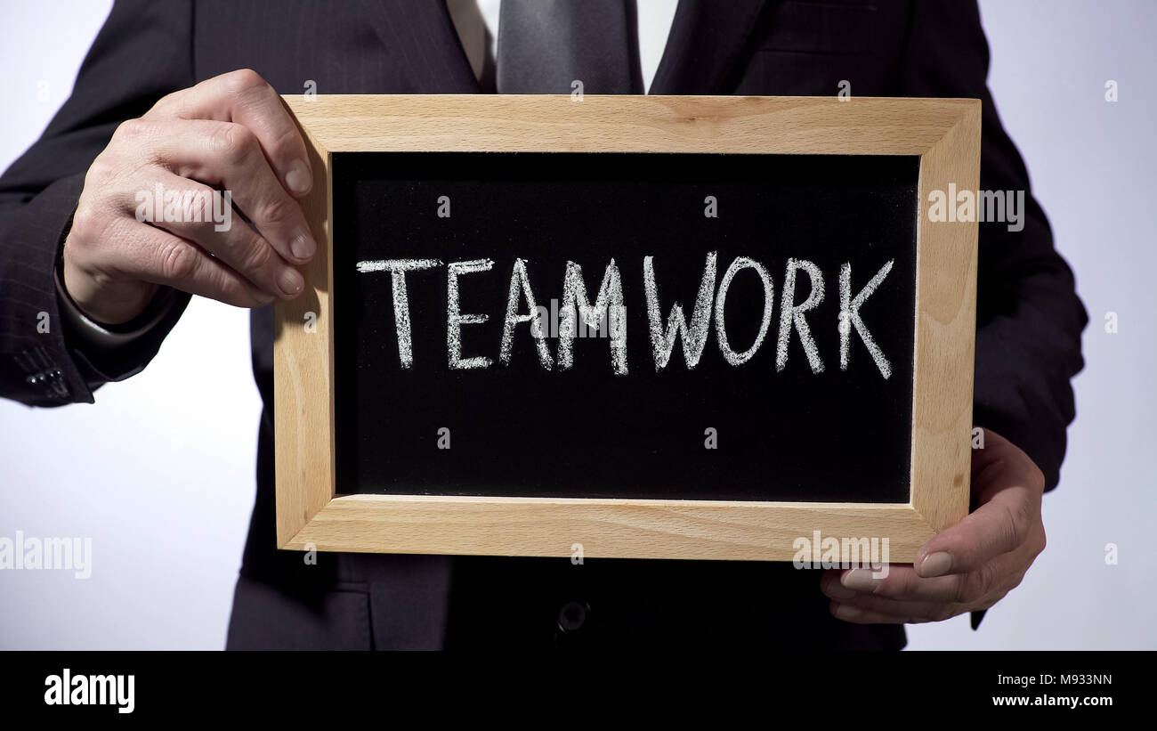 Teamwork written on blackboard, businessperson holding sign in hands ...