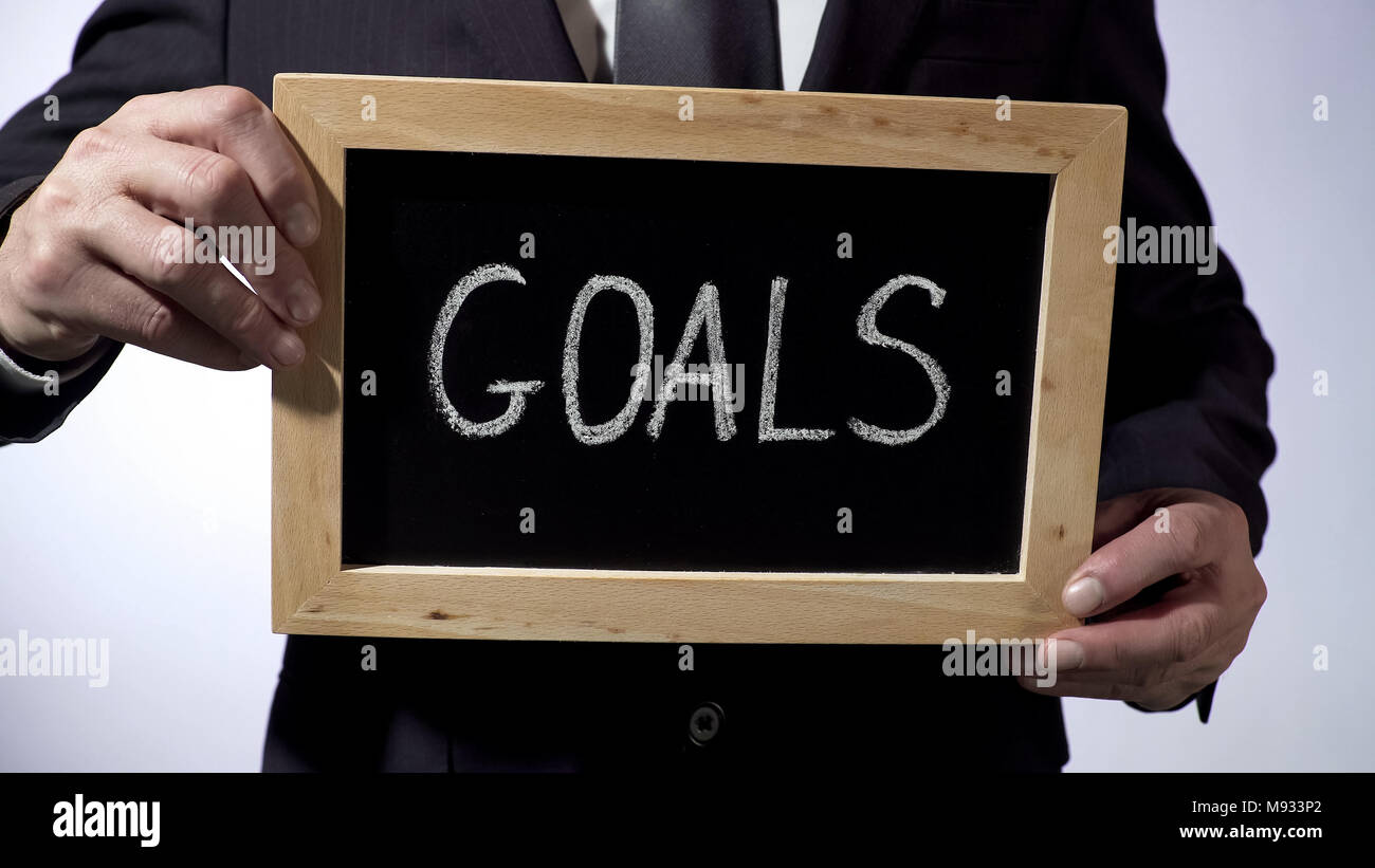 Goals written on blackboard, man in classic suit holding sign, business ...
