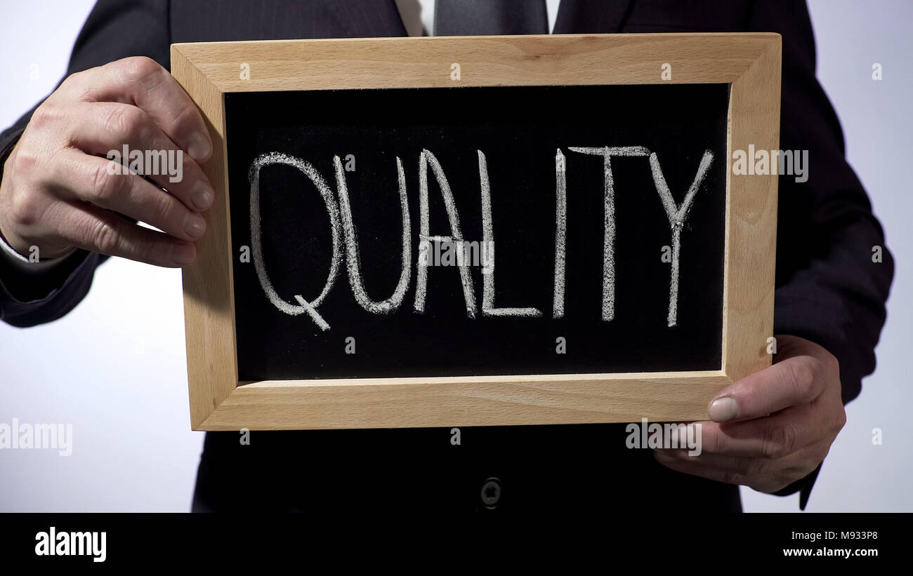 Quality written on blackboard, businessman holding sign, business ...