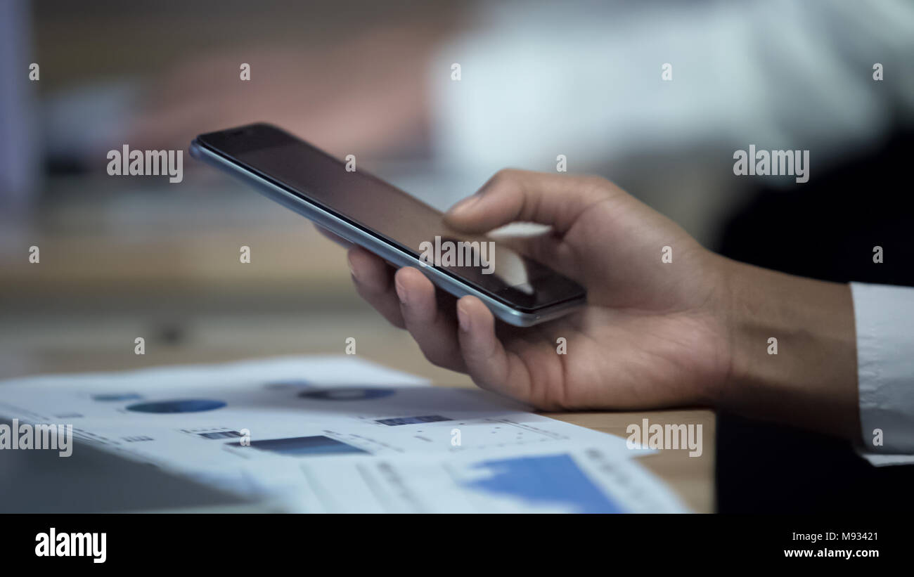Office worker using smartphone while observing charts, modern ...