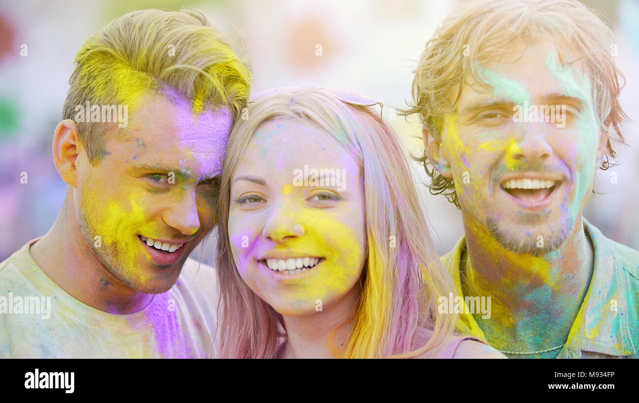 Excited faces of beautiful young people covered in colors smiling at ...