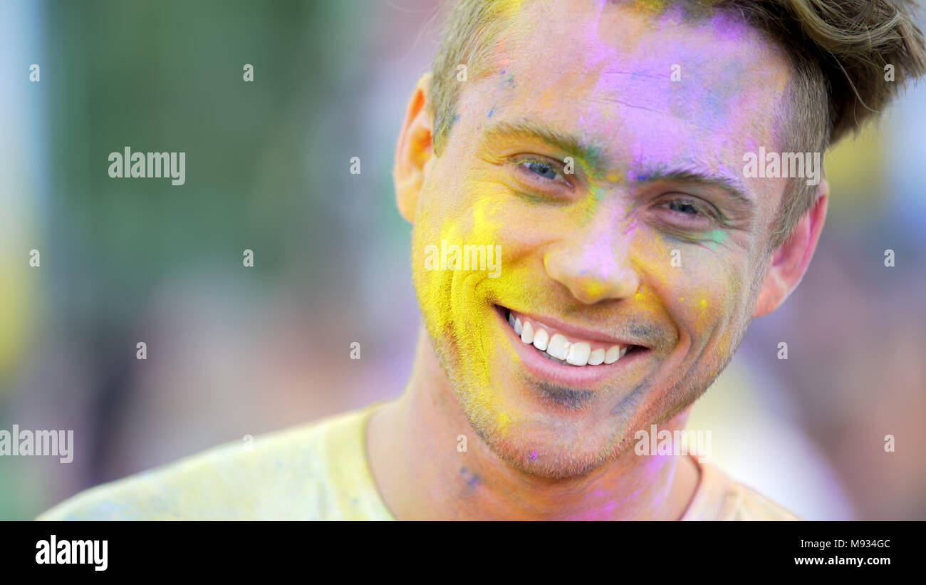 Cheerful face of young handsome man in coloured powder smiling to ...