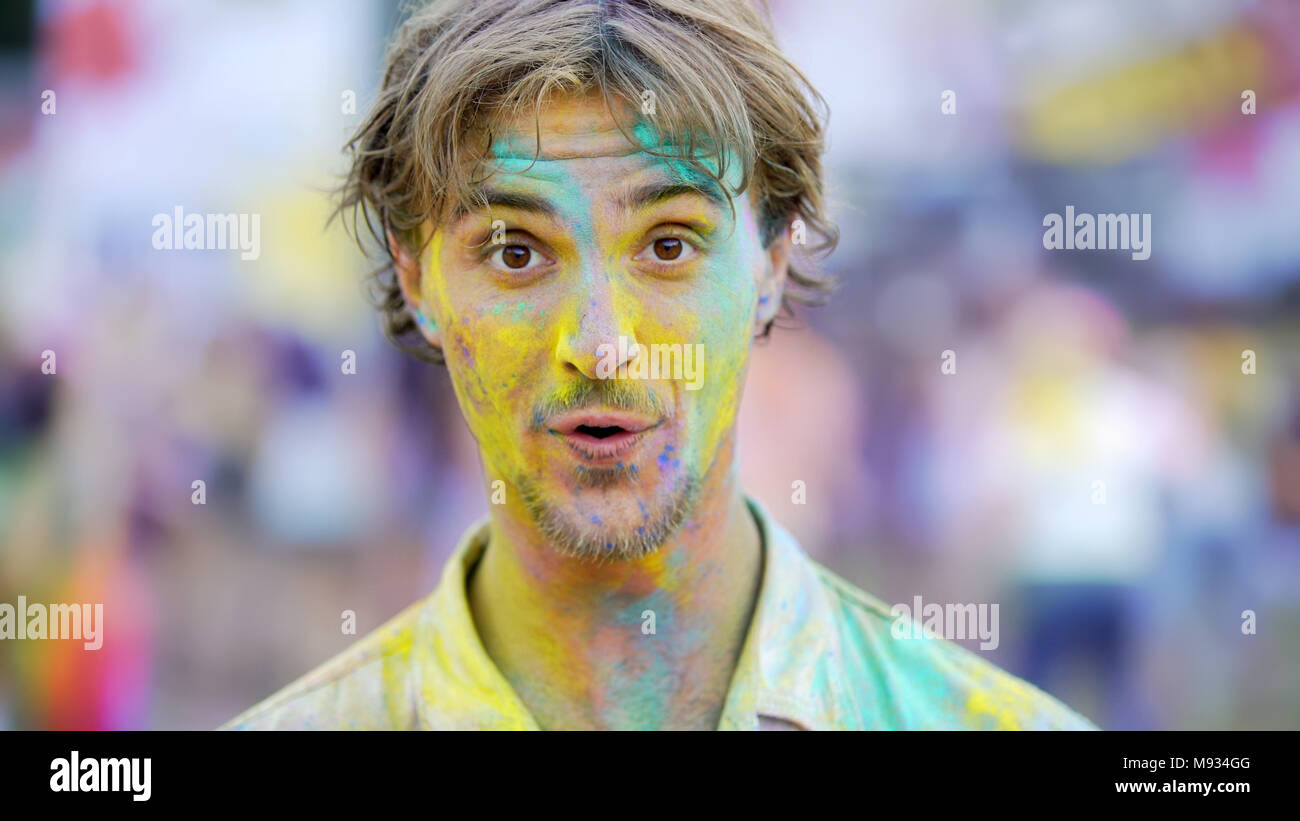 Surprised young man covered in colorful dyes enjoying atmosphere at ...