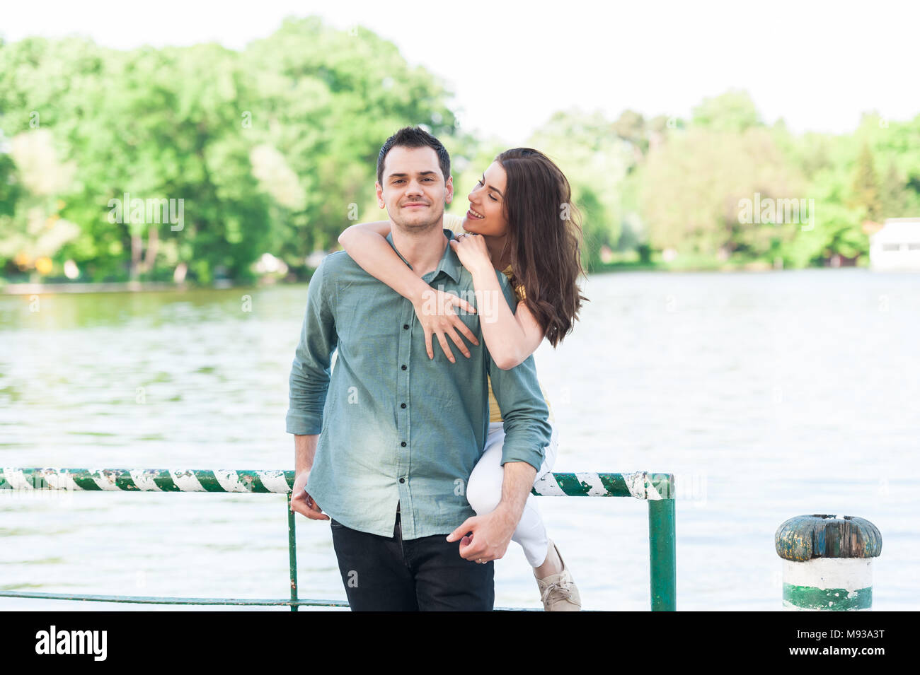 Joyful and spontaneous couple in love, holding hands on a stone pier on a natural lake having ...